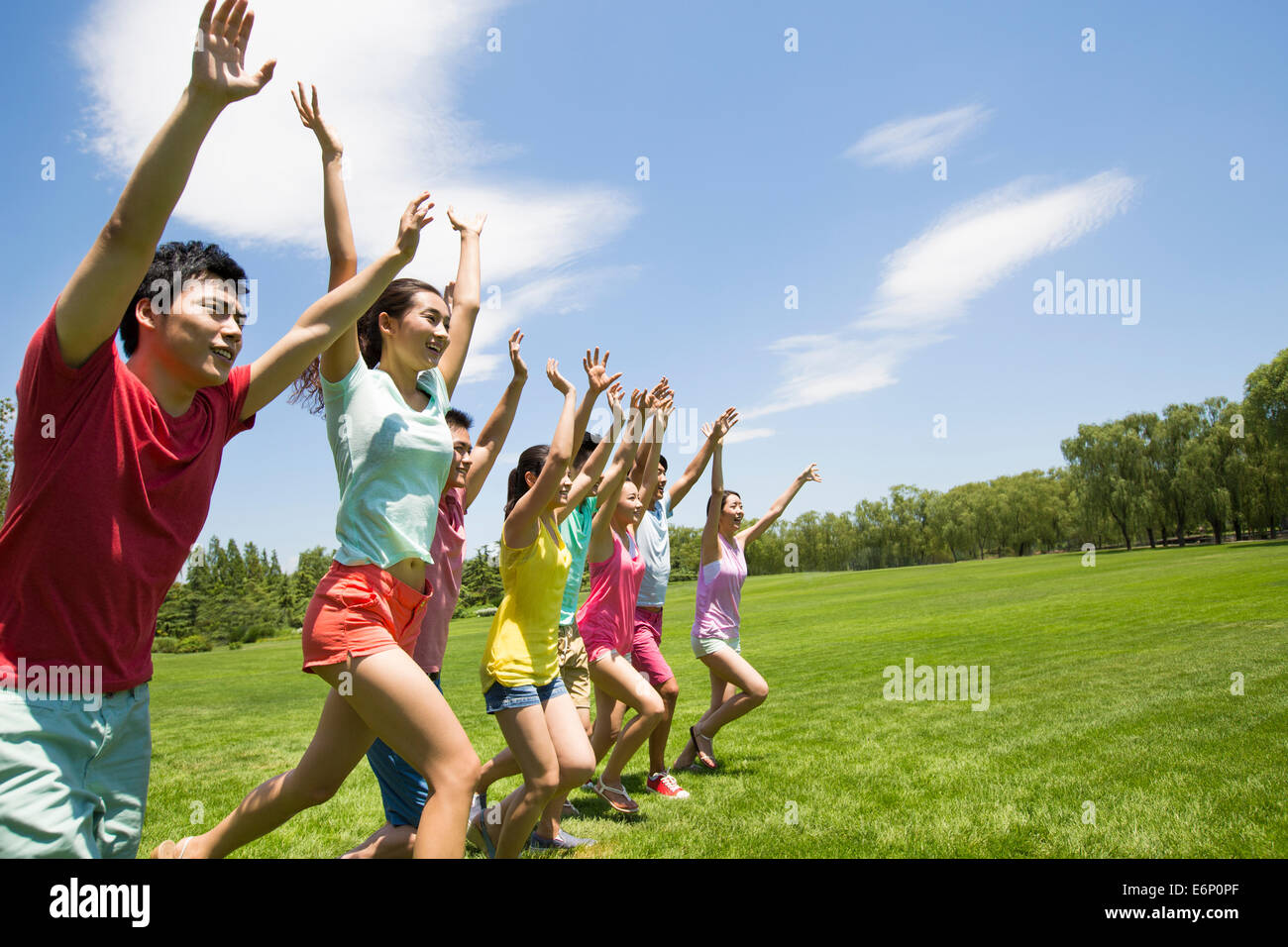 Cheerful young adults raising arms running on grass Stock Photo - Alamy