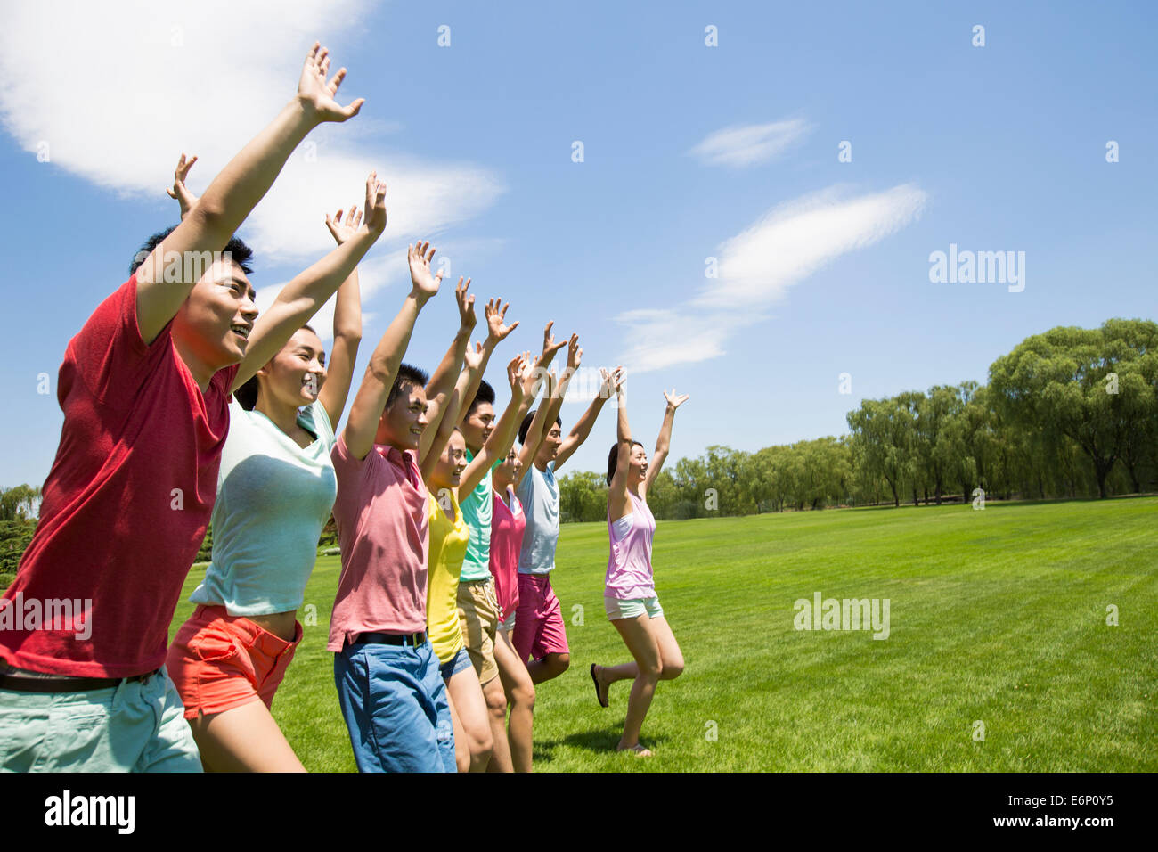 Cheerful young adults raising arms running on grass Stock Photo - Alamy