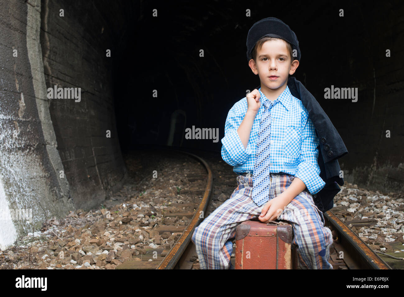 Child in vintage clothes sits on railway road in front of a tunnel ...