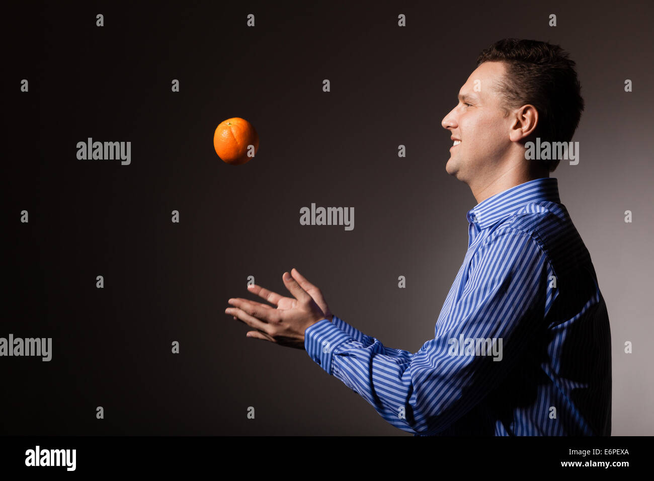 Diet and nutrition. Young smiling man throwing orange tropical fruit on ...