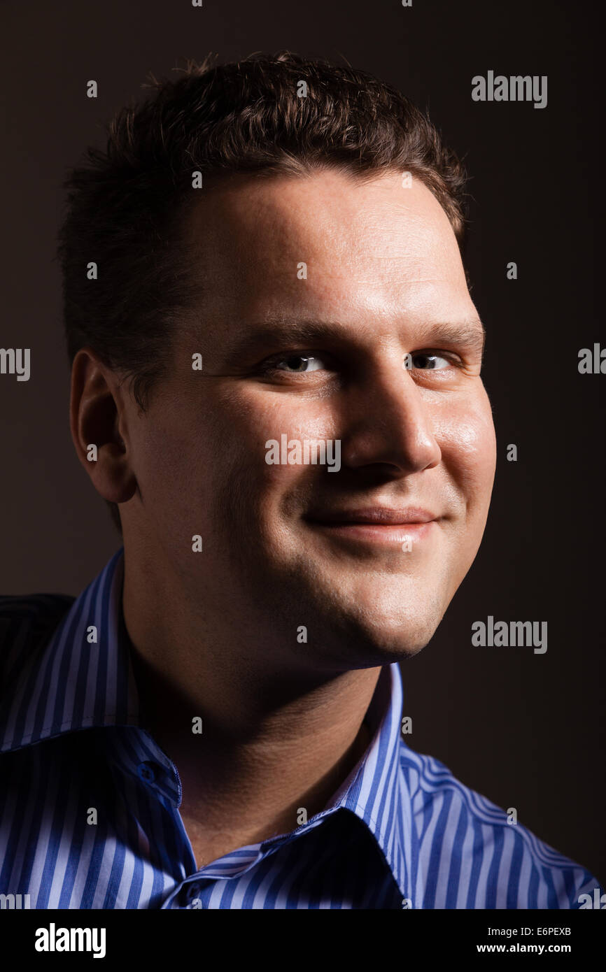 Portrait of happy young man in blue shirt on dark gray. Face of smiling ...