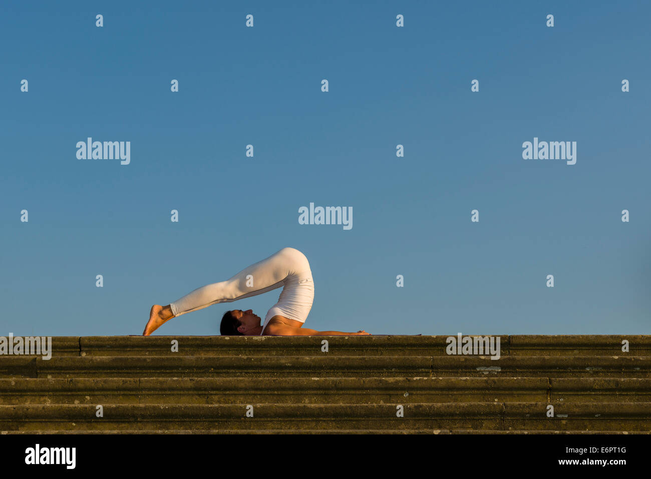 Young woman practising Hatha yoga, outdoors, showing the pose Halasana ...