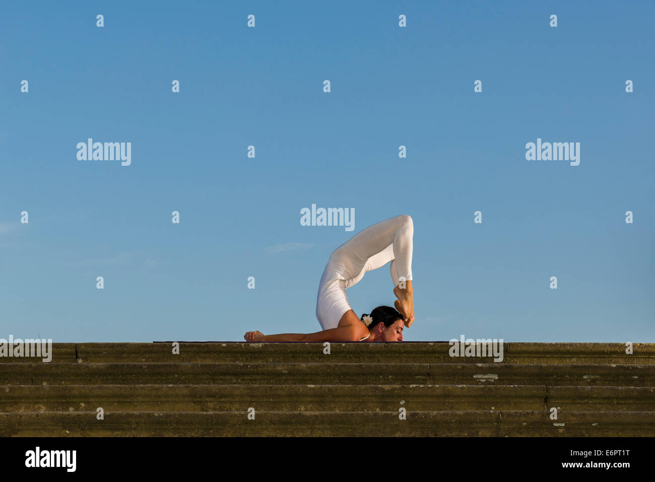 Young woman practising Hatha yoga, outdoors, showing the pose poorna ...