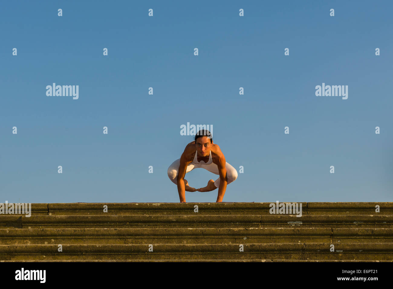 Young woman practising Hatha yoga, outdoors, showing the pose Kakasana ...