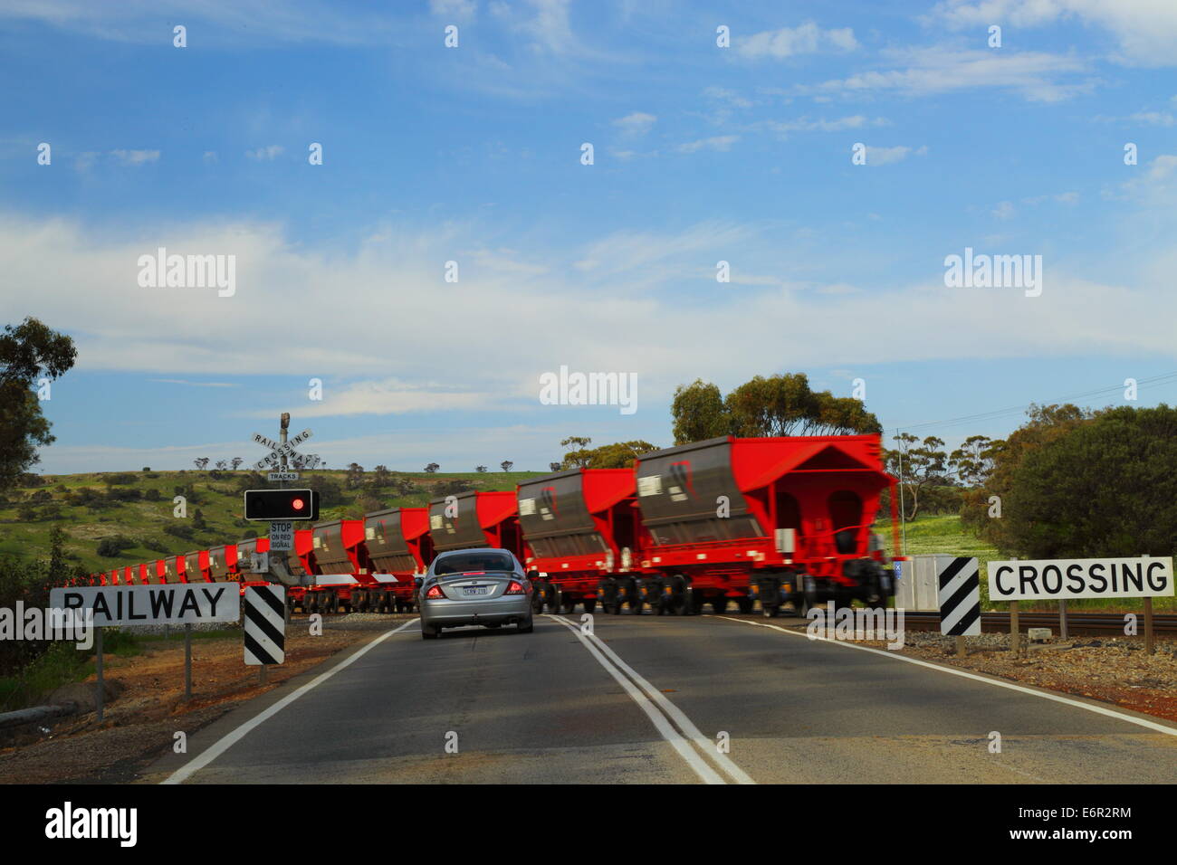 A car waits at a railway crossing as a freight train with grain bins ...