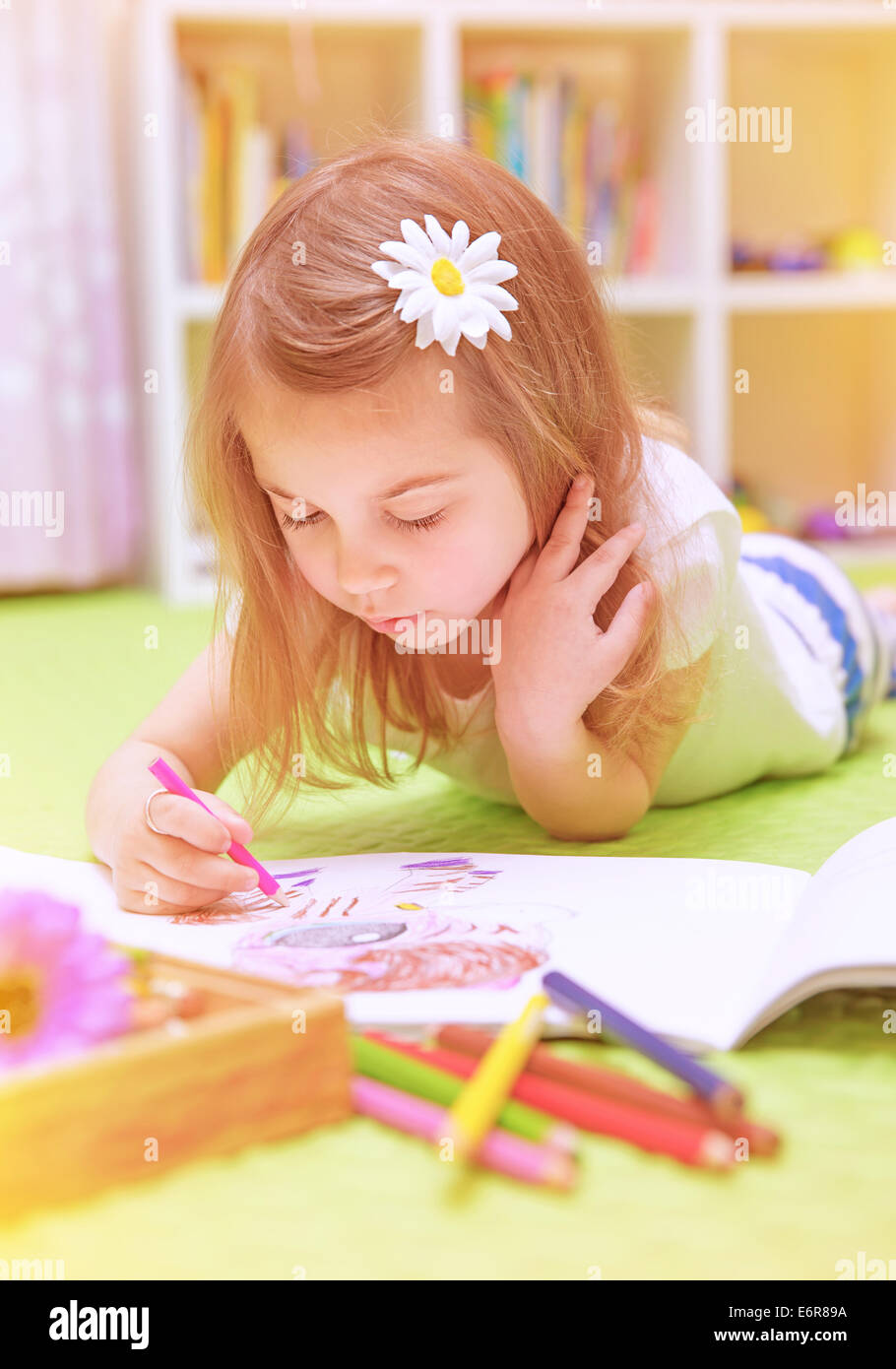 Preschooler girl painting with colorful pencil, lying down on the floor ...