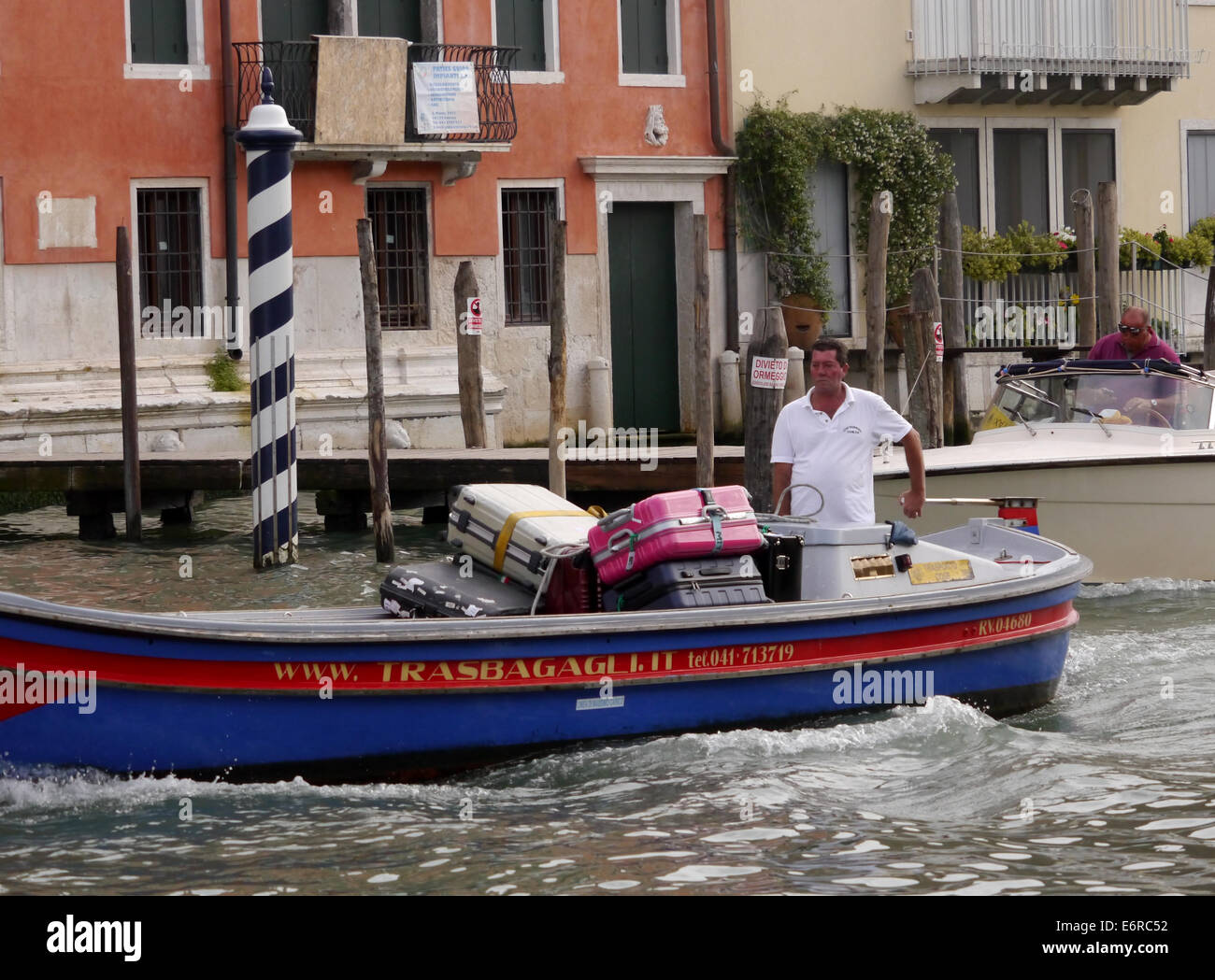 Man driving boat in Venice carrying suitcases along canal Stock Photo ...