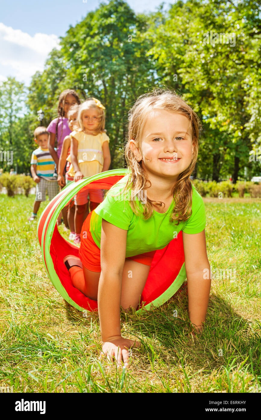 Happy girl crawl through play tube with friends Stock Photo - Alamy
