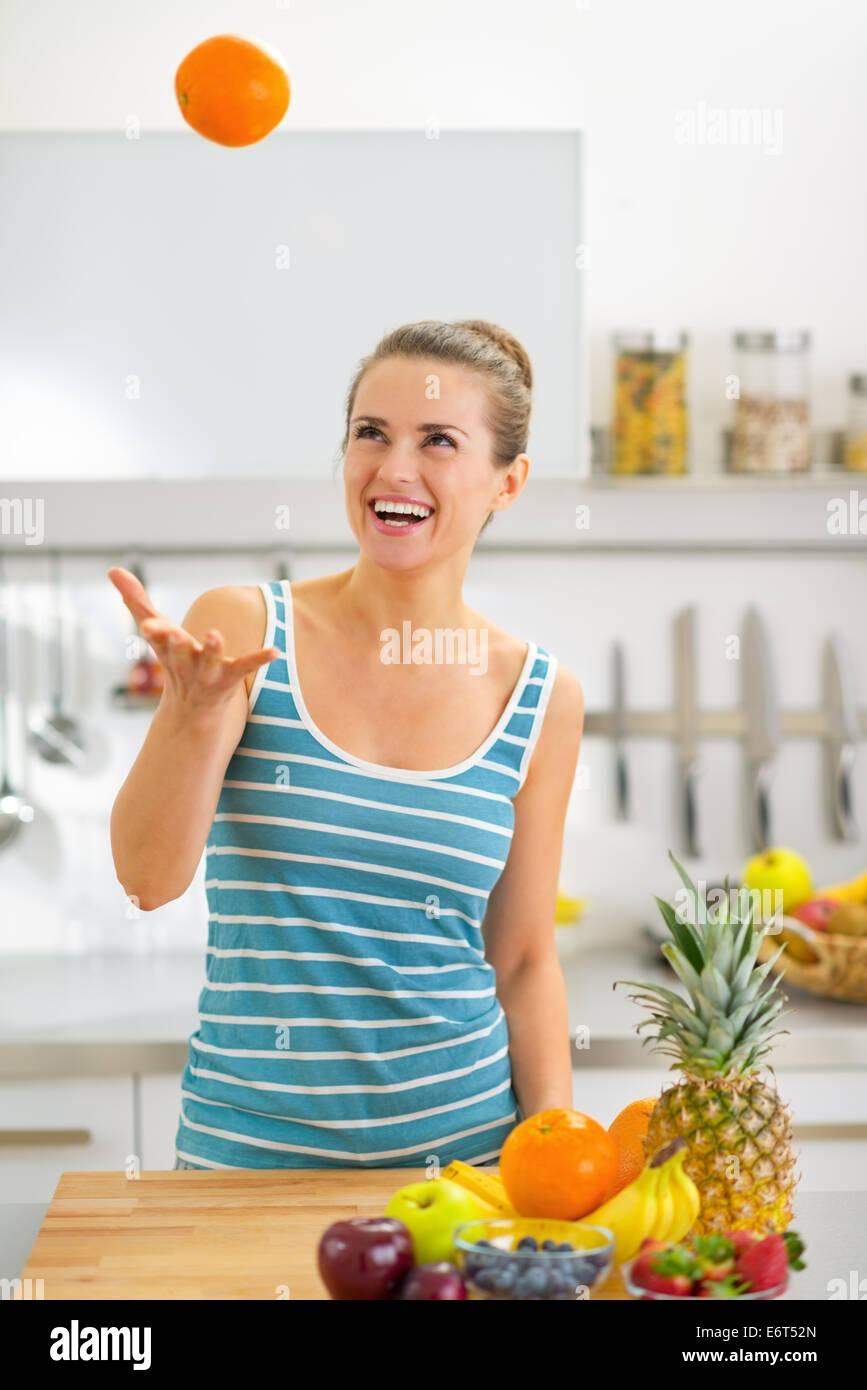 Young woman throwing orange up in kitchen Stock Photo - Alamy