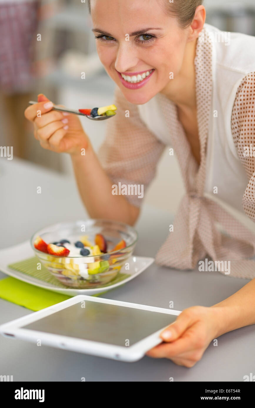 Happy young woman eating fruit salad and using tablet pc Stock Photo ...