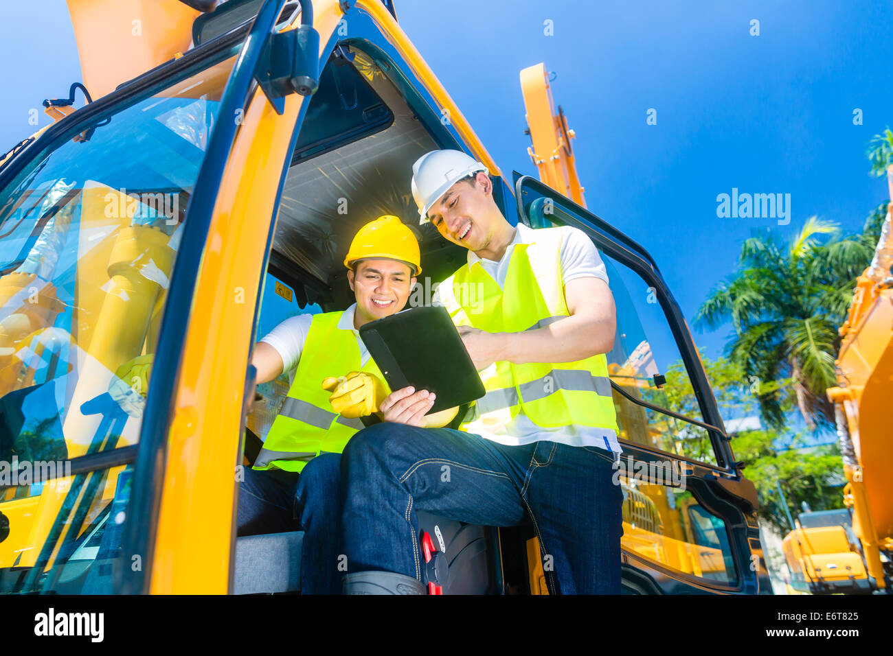 Asian construction machinery driver discussing with foreman blueprints ...