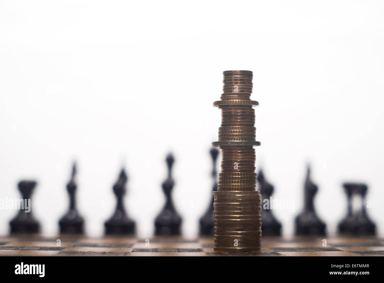 Euro or dollar coins stacked like a king on a chess board on a white ...