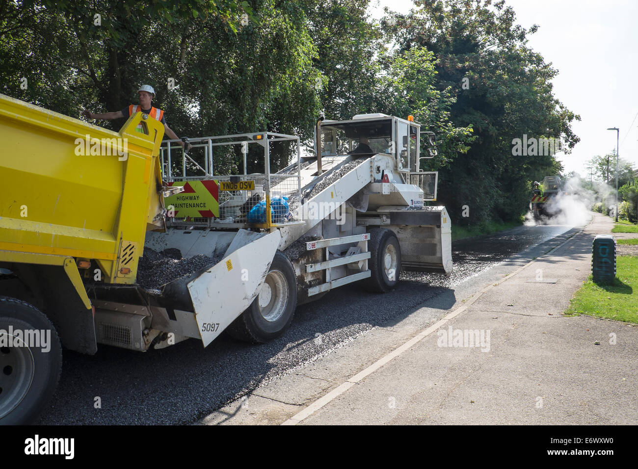 Tipper lorry loading granite chippings into hopper on chipping spreader ...