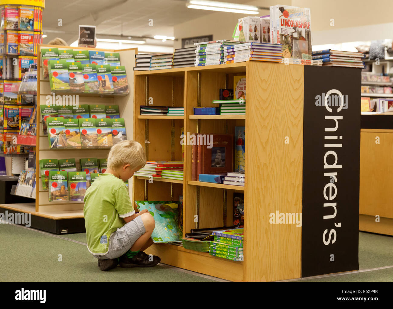 A child reading a book in a bookshop, in the childrens books section ...