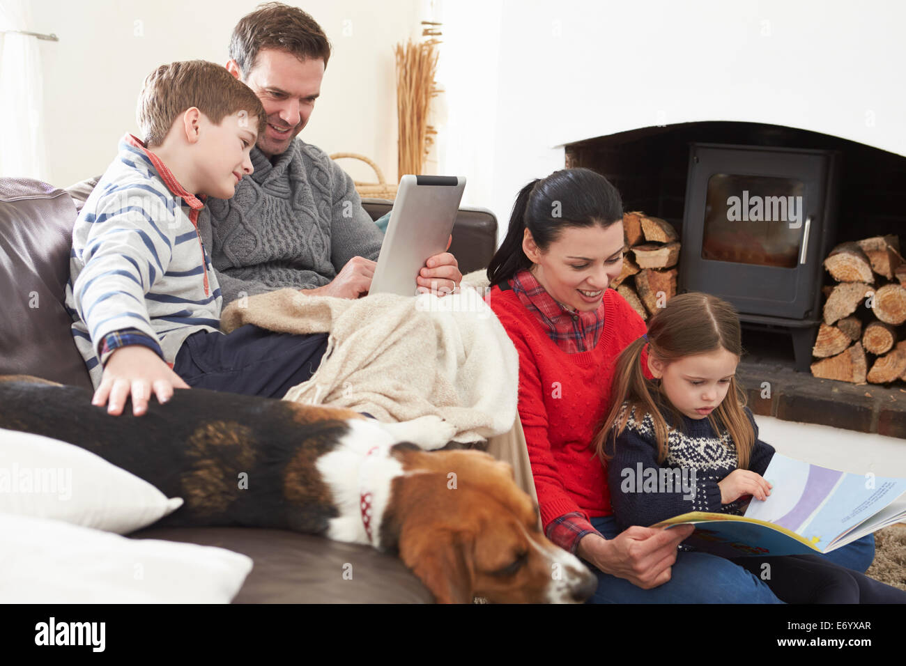 Family Relaxing Reading Book And Using Digital Tablet Stock Photo - Alamy