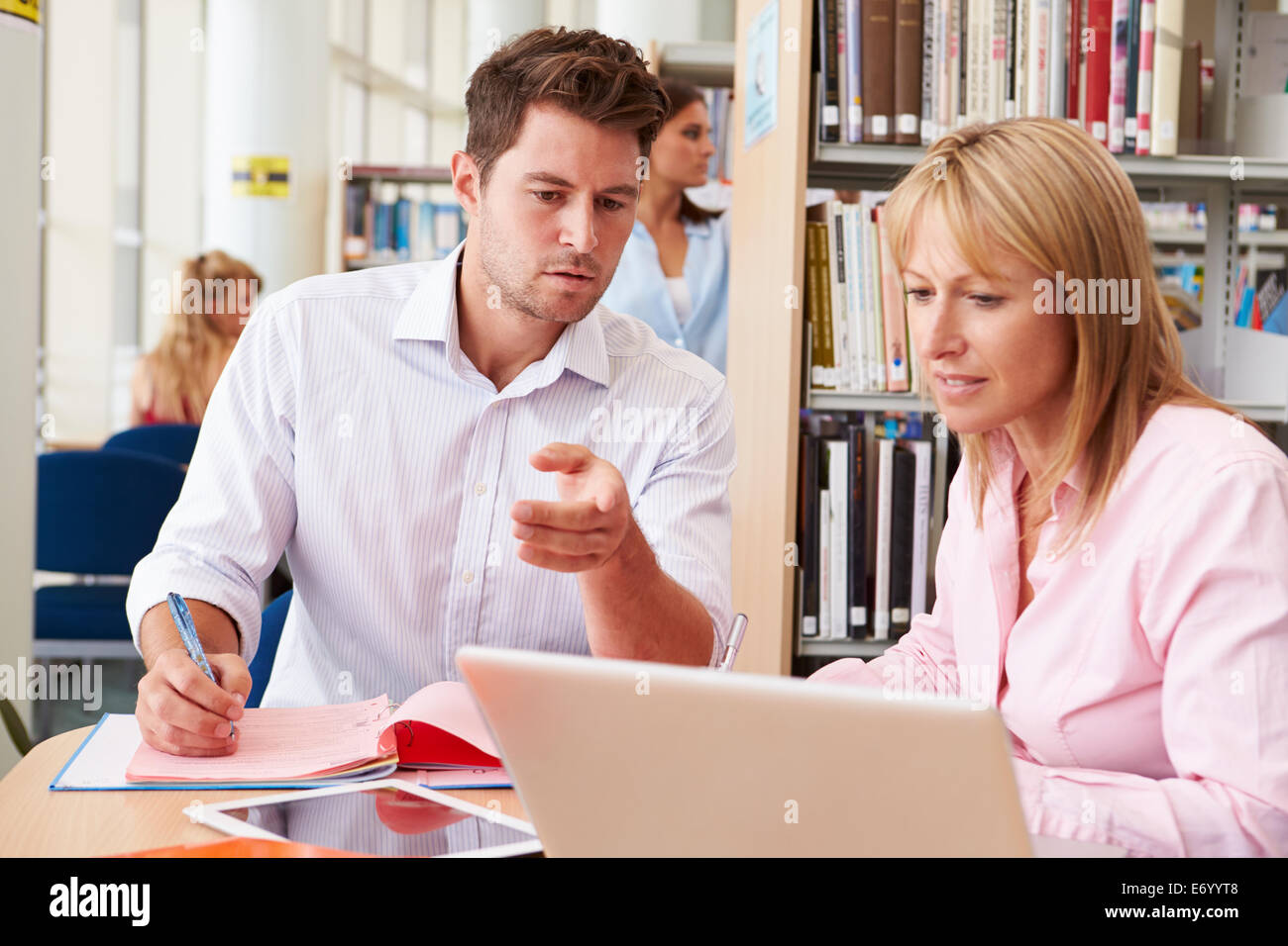 Teacher Helping Mature Student With Studies In Library Stock Photo - Alamy
