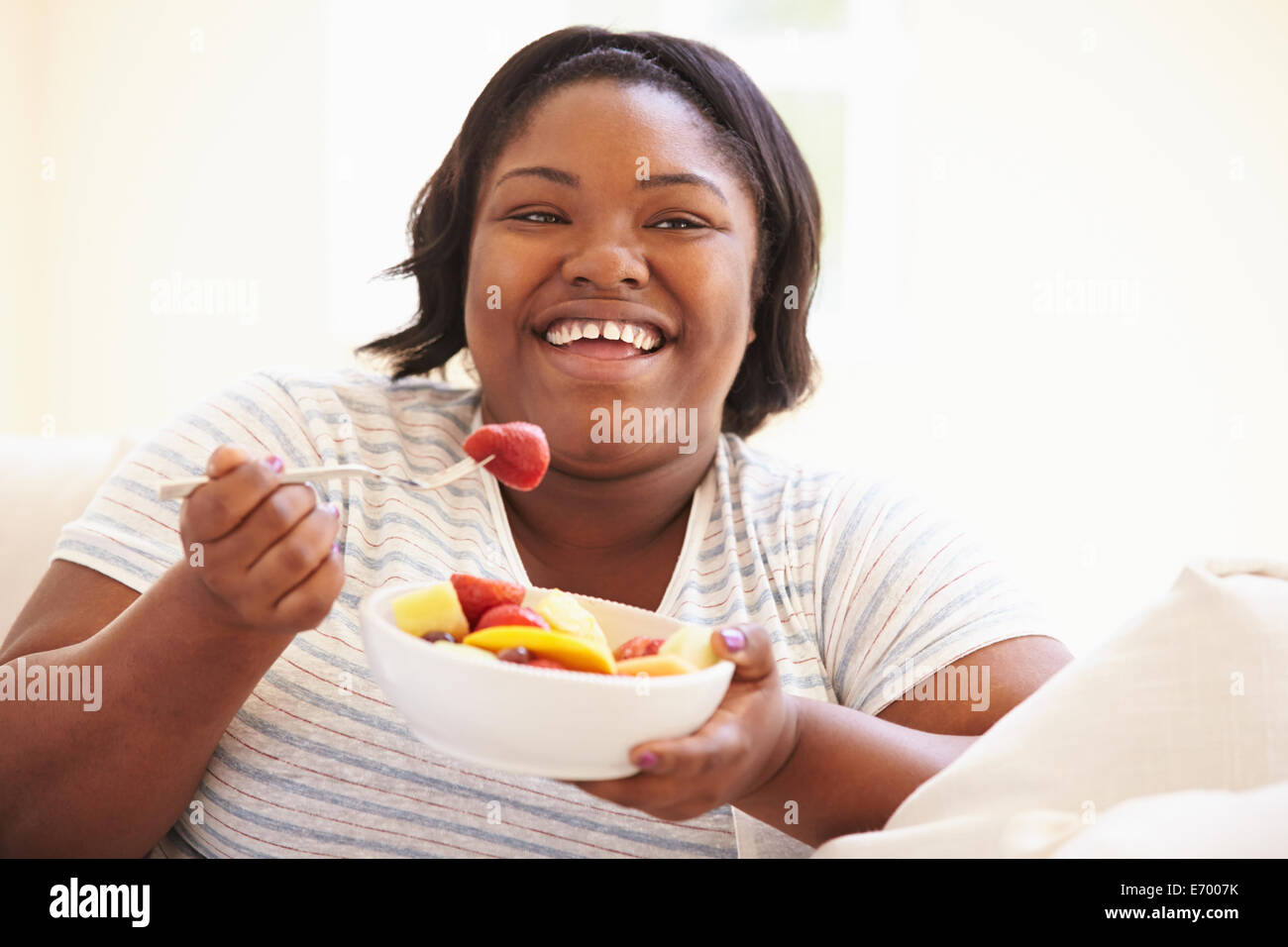 Overweight Woman Sitting On Sofa Eating Bowl Of Fresh Fruit Stock Photo ...