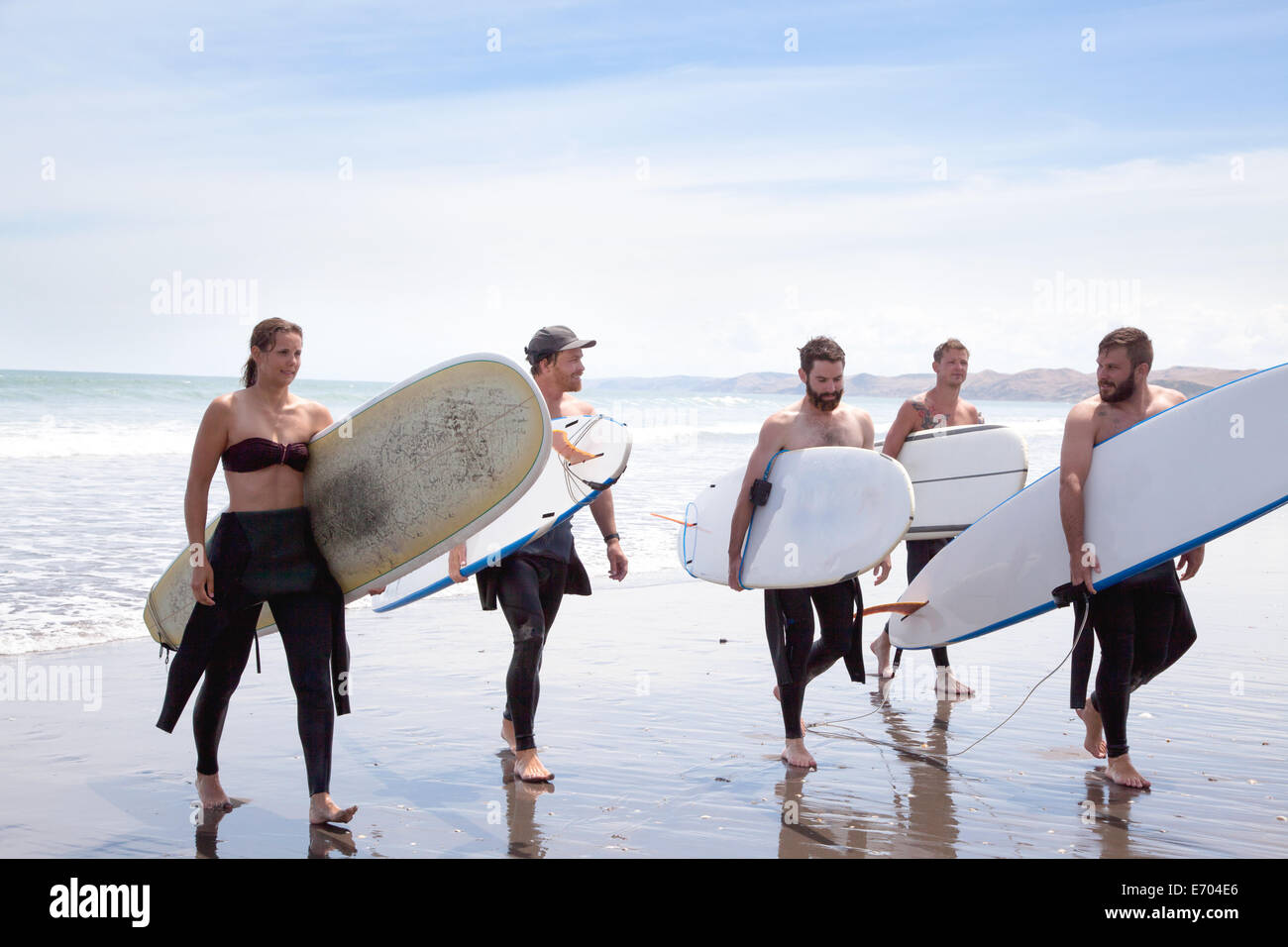 Group of male and female surfer friends walking away from sea with surf ...