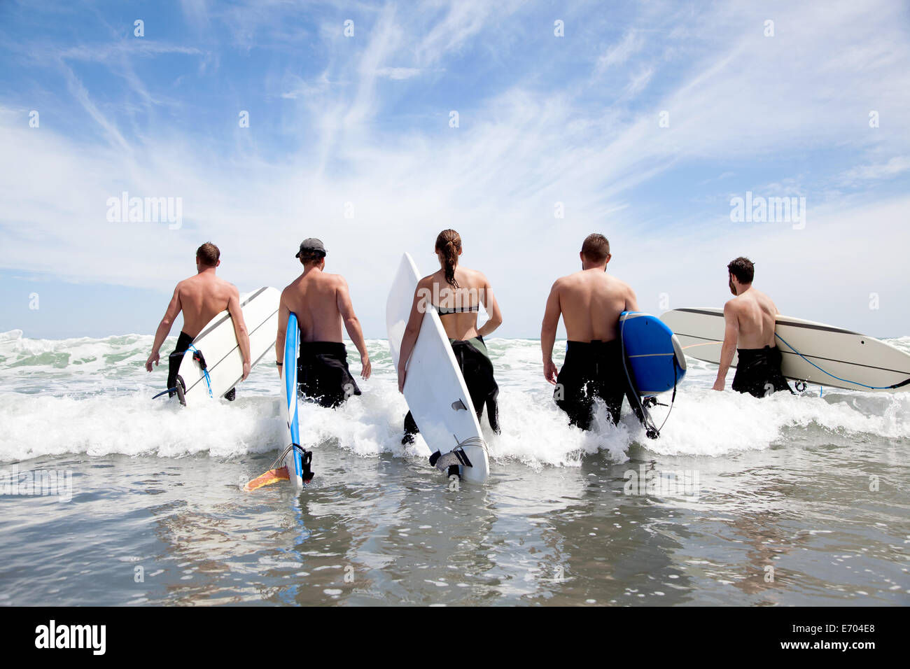 Rear view of a group of male and female surfer friends wading into sea ...