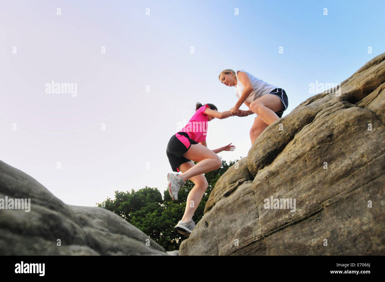 Two young women runners helping each other on top of rock formation ...