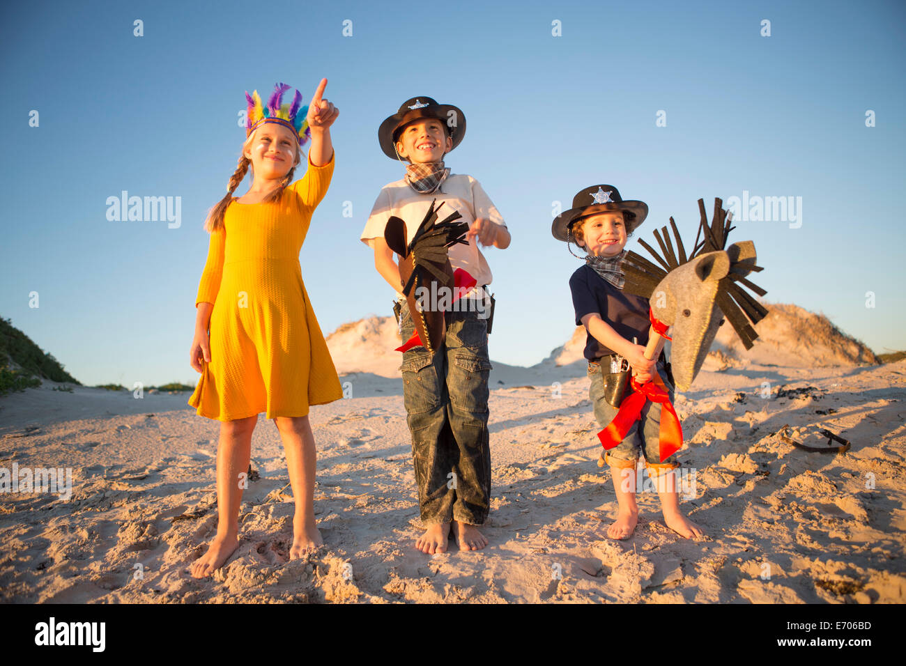 Sister and brothers dressed as native american and cowboys pointing ...