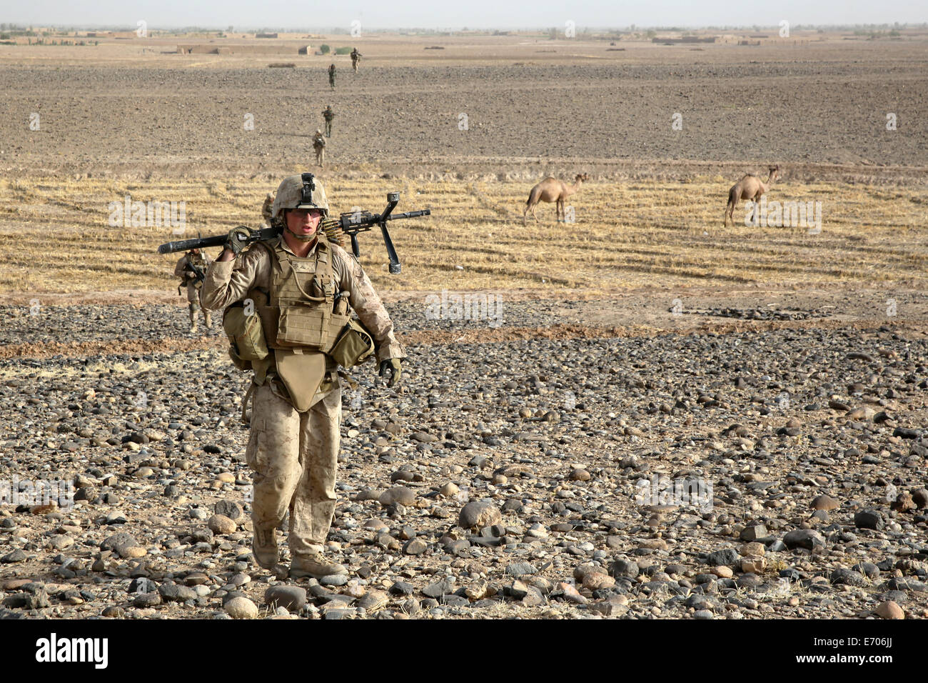 A US Marines carries a M240B medium machine gun across a field during a ...