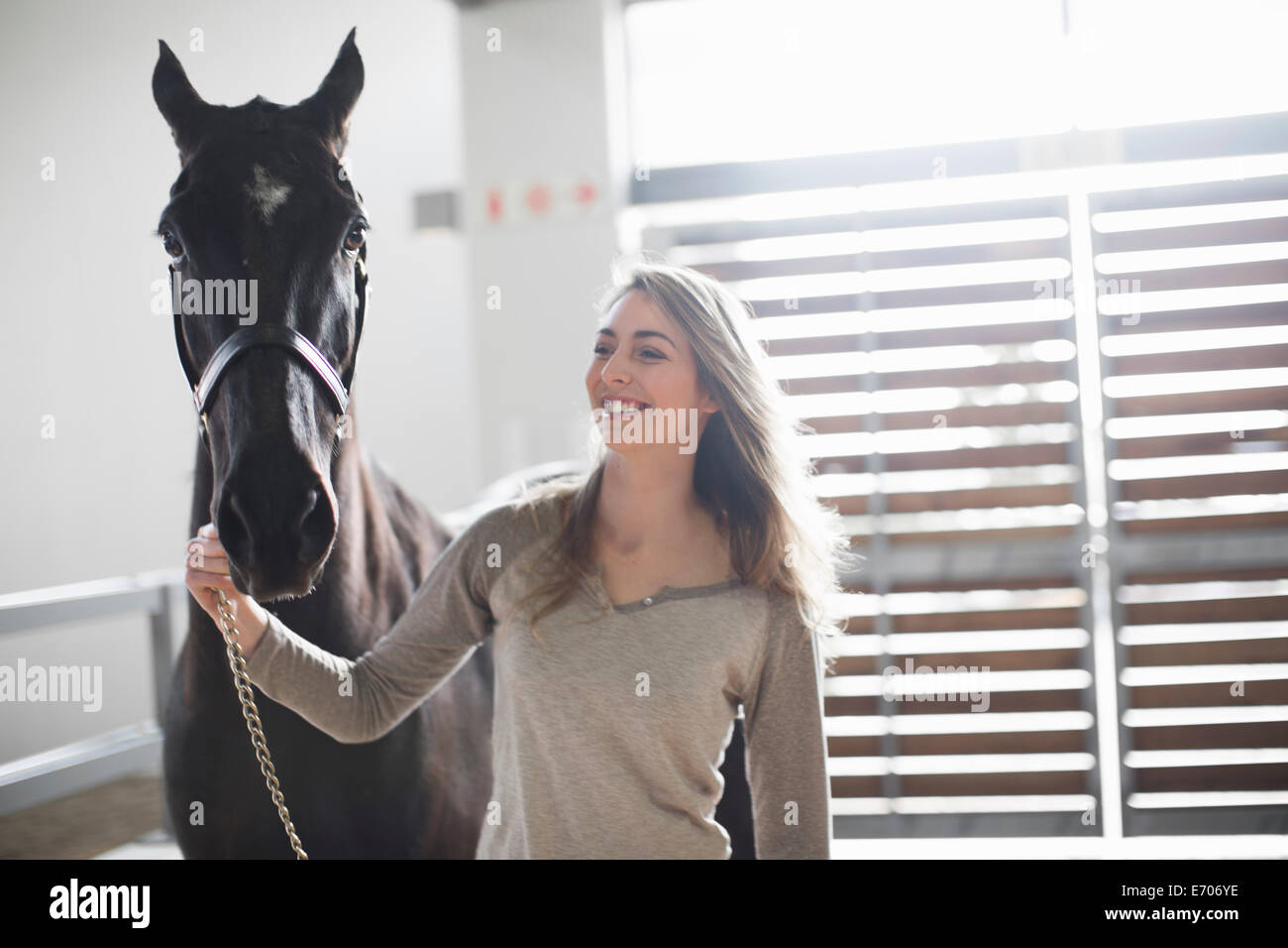 Young woman leading black horse in stables Stock Photo - Alamy