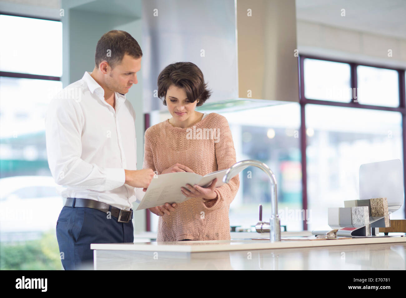 Female customer and salesman looking at brochure in kitchen showroom ...