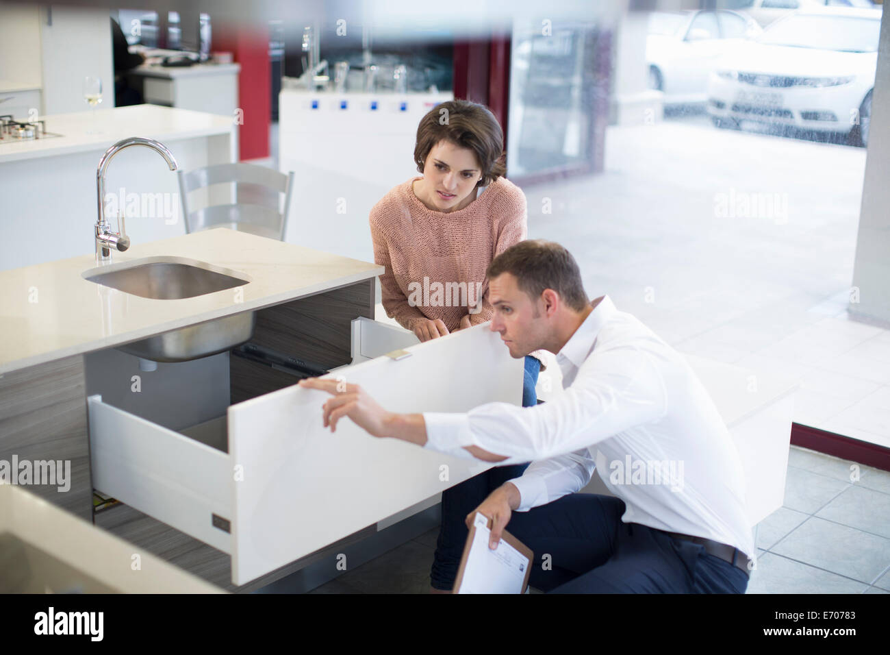 Female customer and salesman looking at drawer in kitchen showroom ...