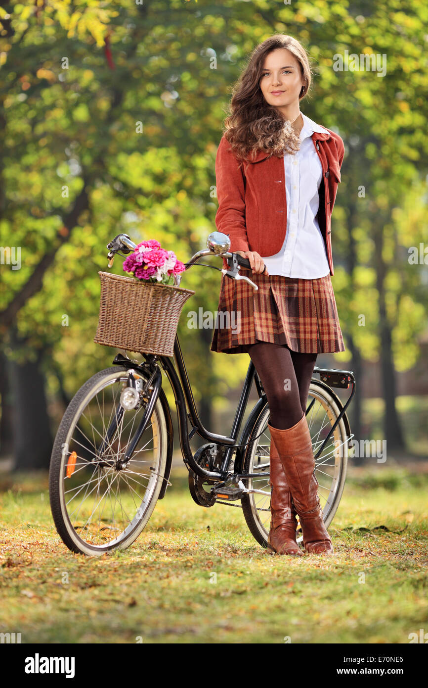 Vertical shot of a fashionable woman posing with her bicycle in park ...