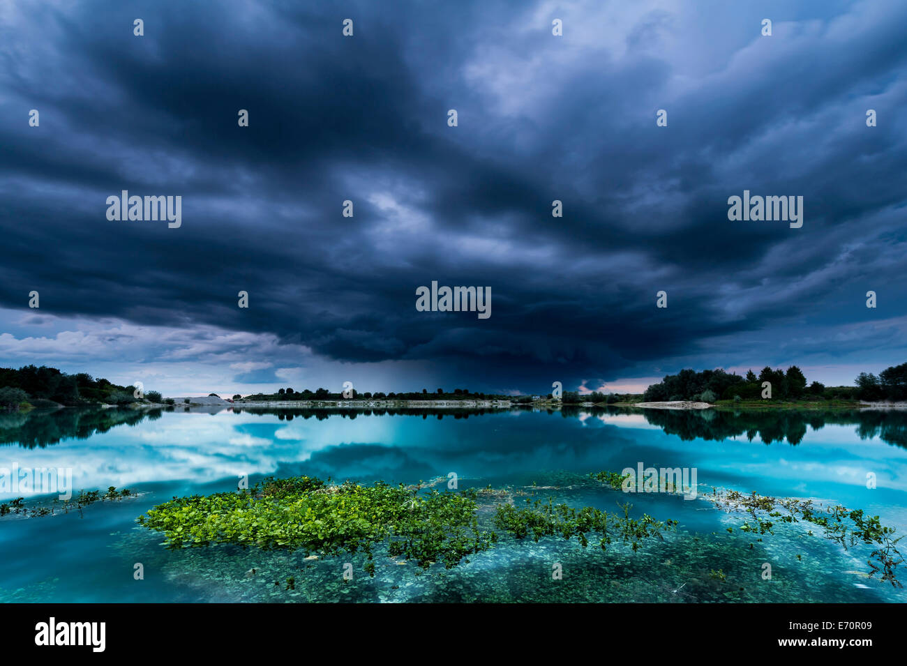 Storm clouds over a quarry lake with water plants, near Mindelheim ...