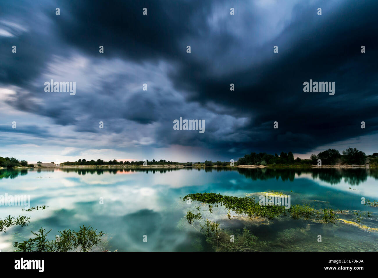 Storm clouds over a quarry lake with water plants, near Mindelheim ...