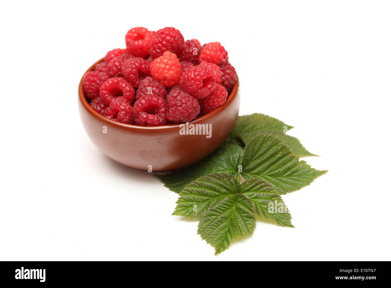 Red raspberries in bowl and strawberry leaves on white background ...