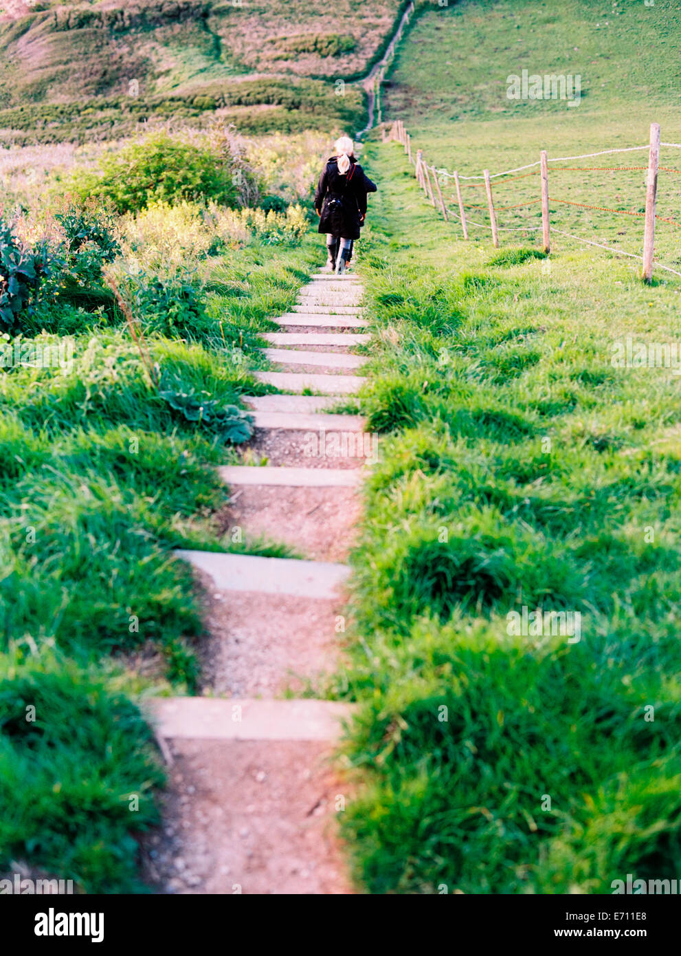Two women walking along a cliff path, walking down a set of steep steps ...