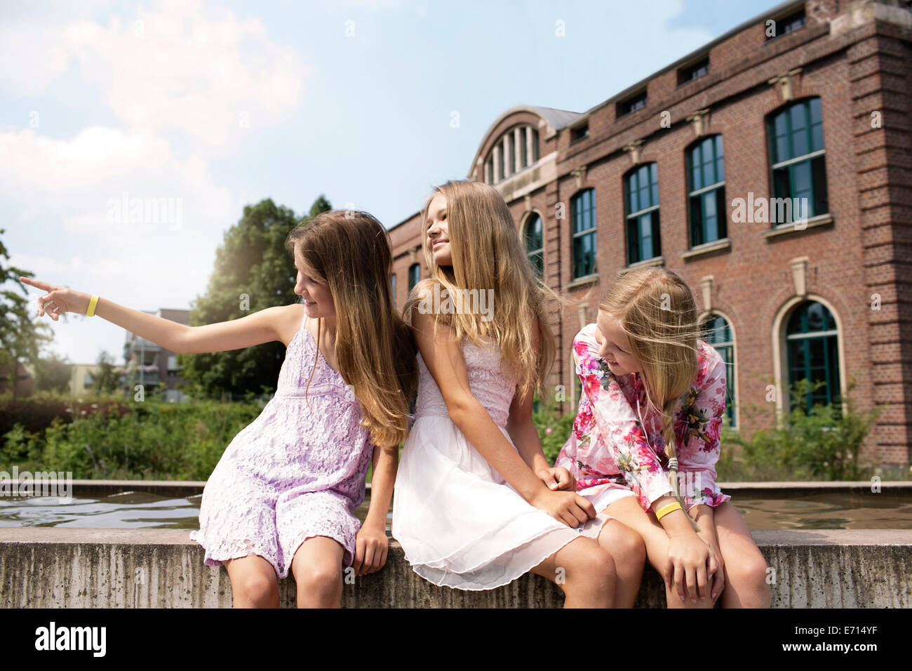 Three girls sitting on a wall watching something Stock Photo - Alamy