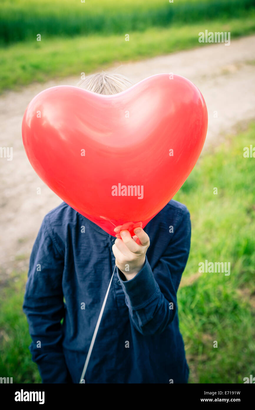 Little boy hiding his face behind a red heart-shaped balloon Stock ...