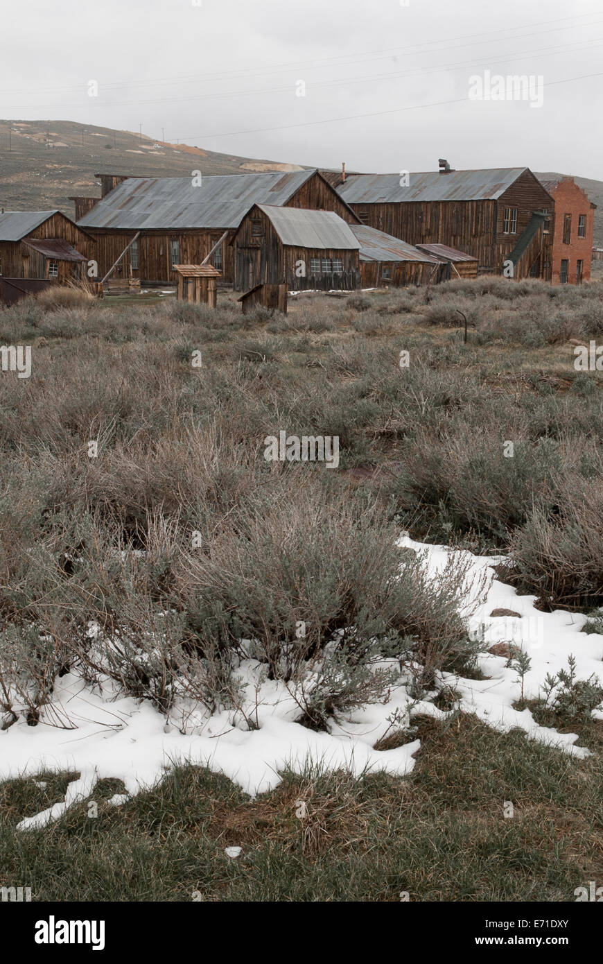 View across melting snow and shrubland to main buildings of Bodie, gold ...