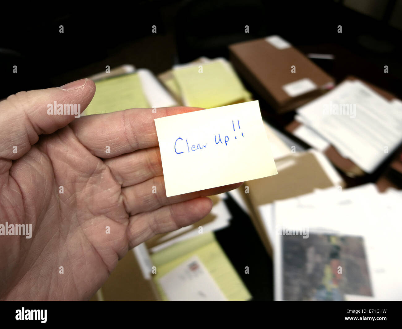 Messy office with hand holding note saying Clean Up Stock Photo - Alamy