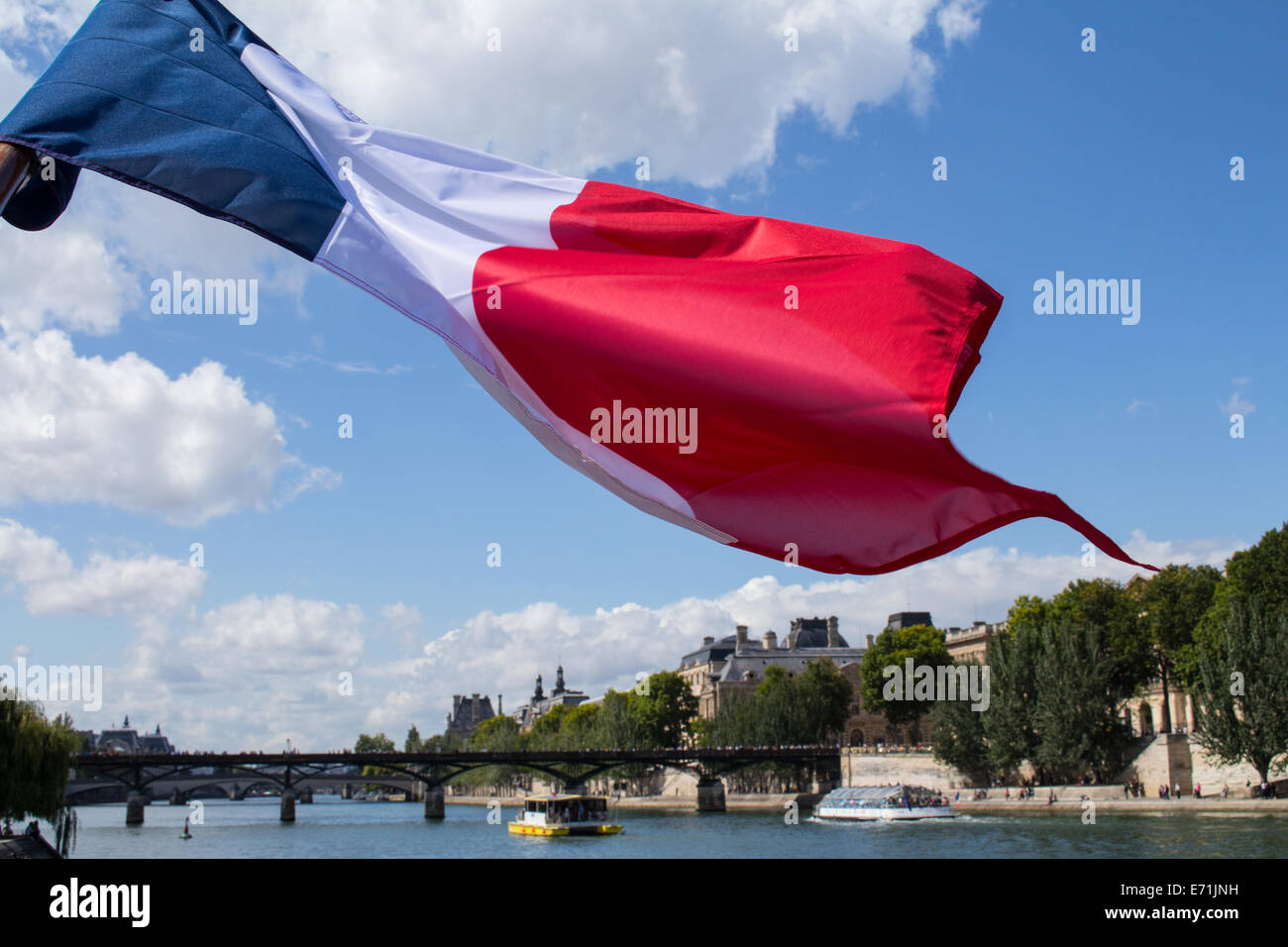 A French Tricolour flag blows in the wind against a cloudy blue sky ...