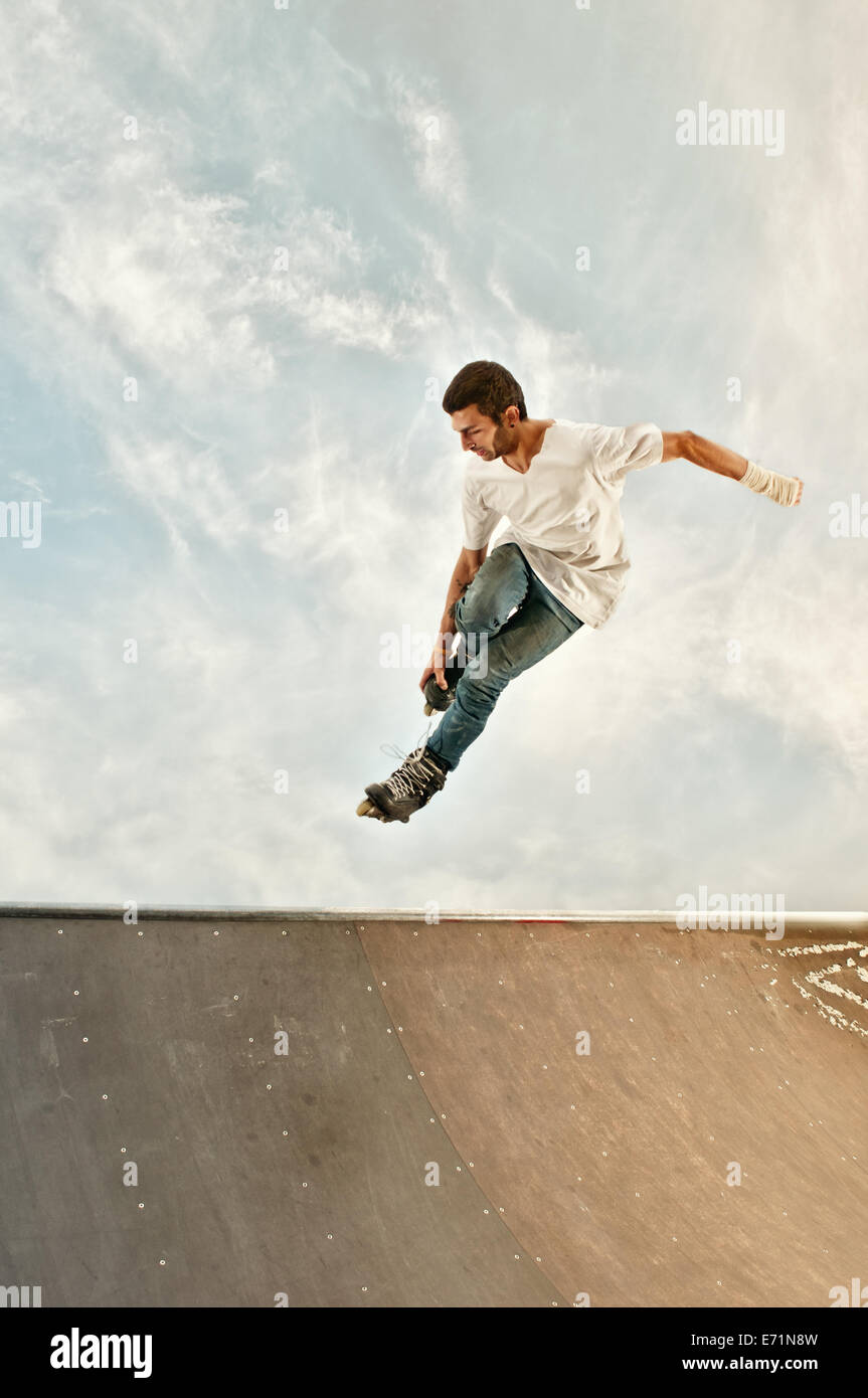 Young man with roller blades jumping high on the skate ramp, frozen in ...