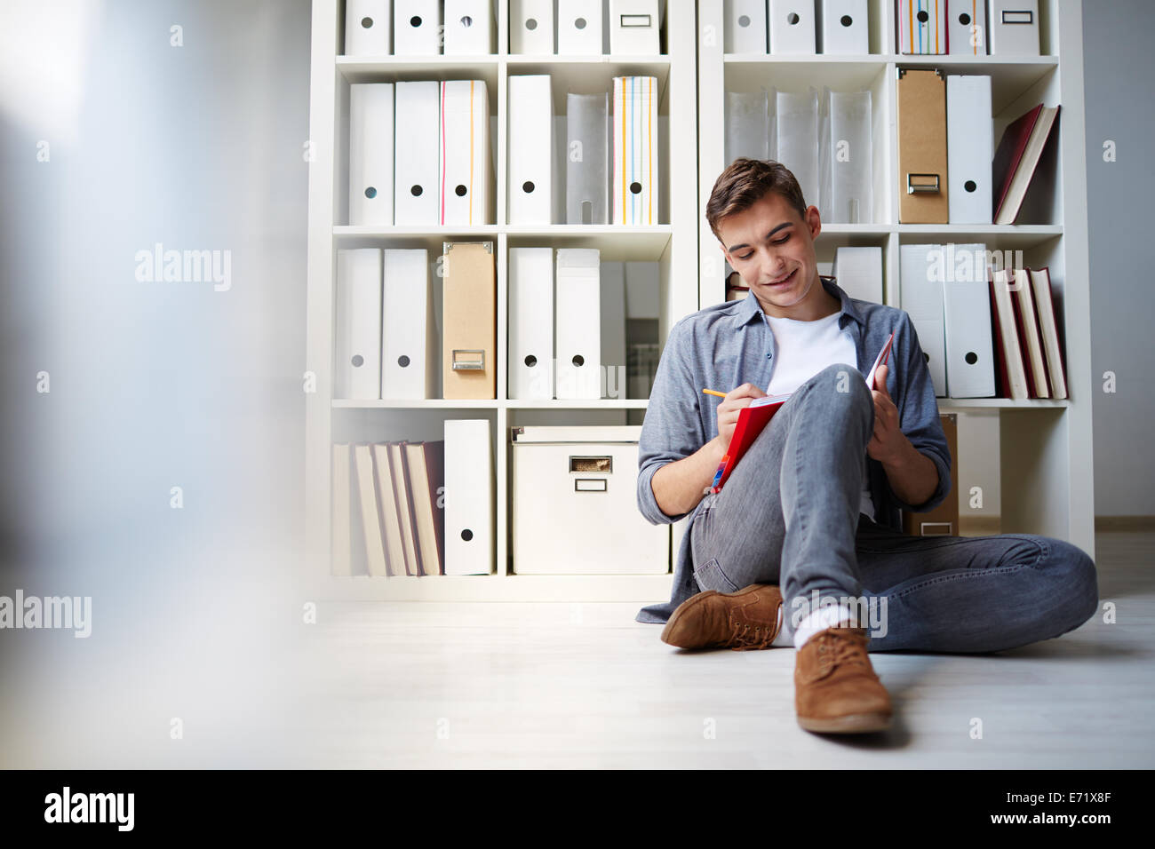 Happy guy sitting on the floor and writing something in notepad Stock ...