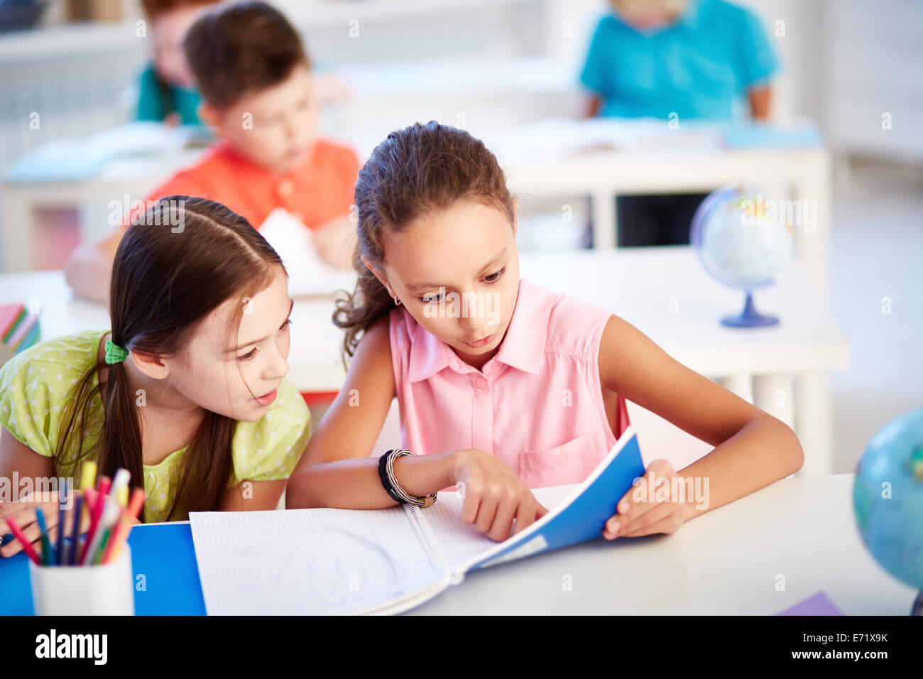Adorable girls discussing something in copybook at lesson Stock Photo ...