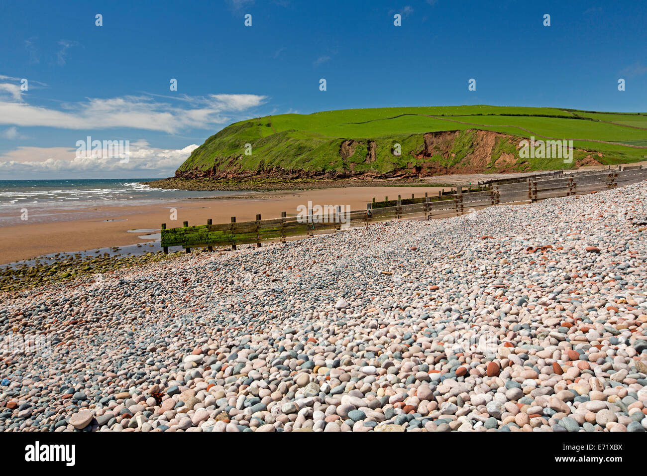 Deserted shingle beach with sand and sea beside green grass covered ...