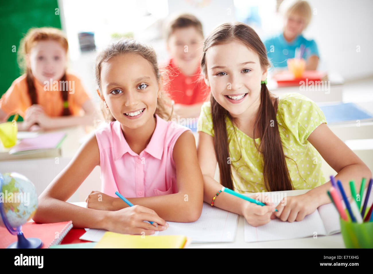 Cute schoolgirls looking at camera on background of other pupils Stock ...