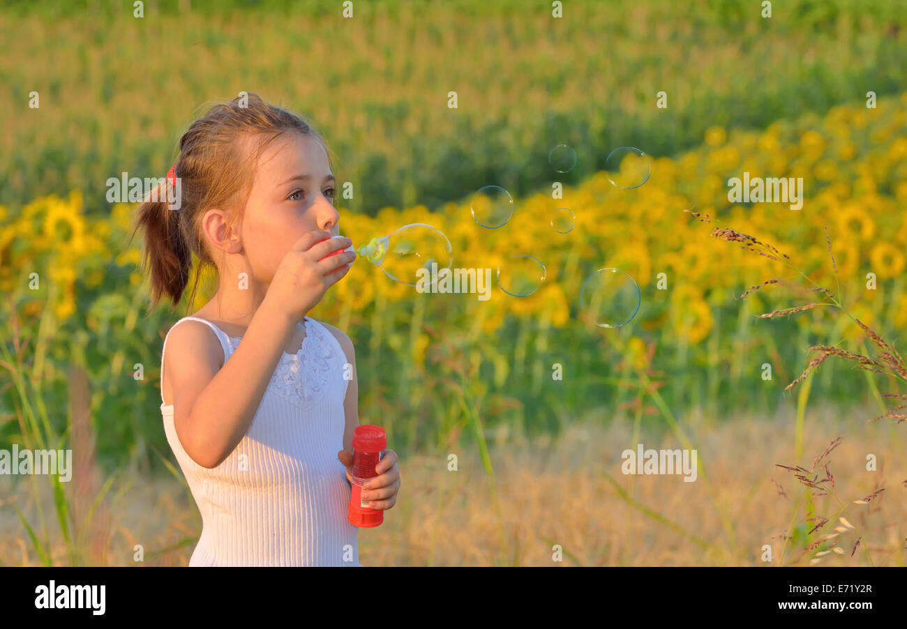 Little girl blowing soap bubbles on field Stock Photo - Alamy