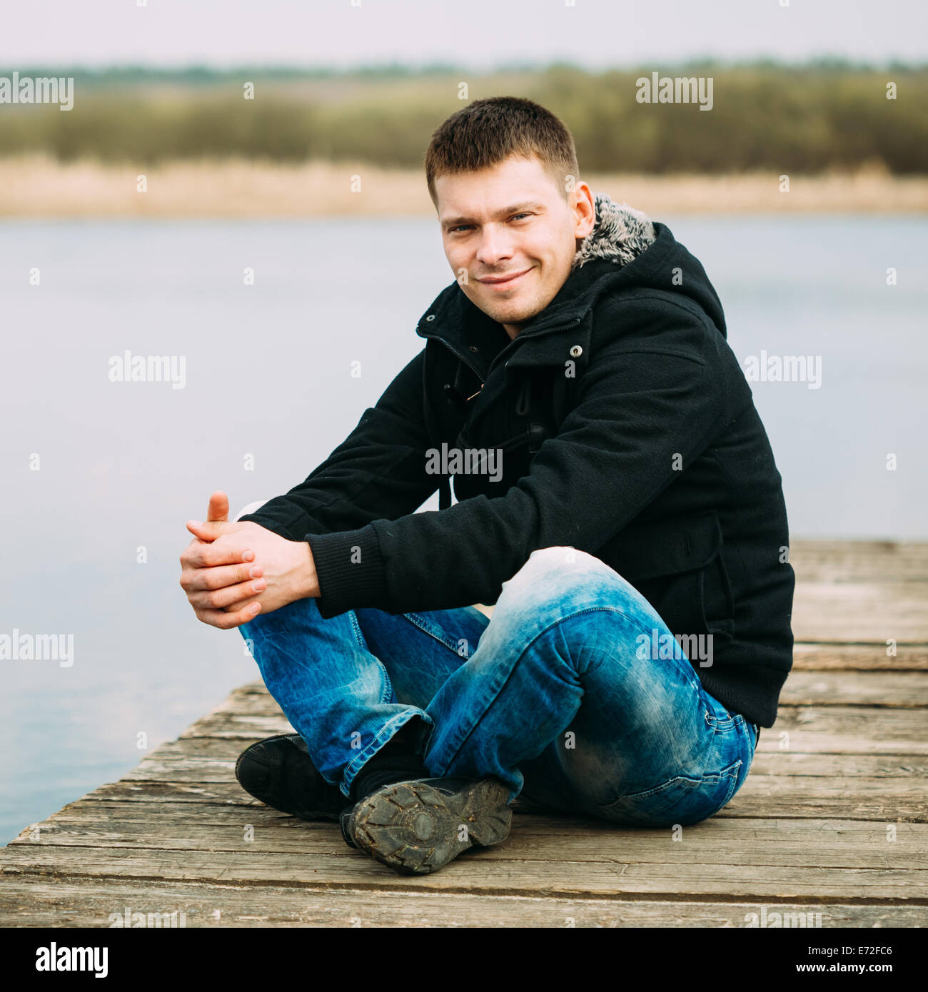 Young handsome man sitting on wooden pier in autumn day, relaxing ...