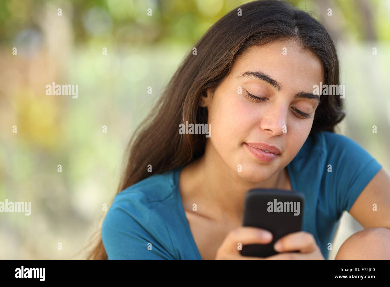 Pretty happy teenager girl texting in a smart phone in a park with a ...