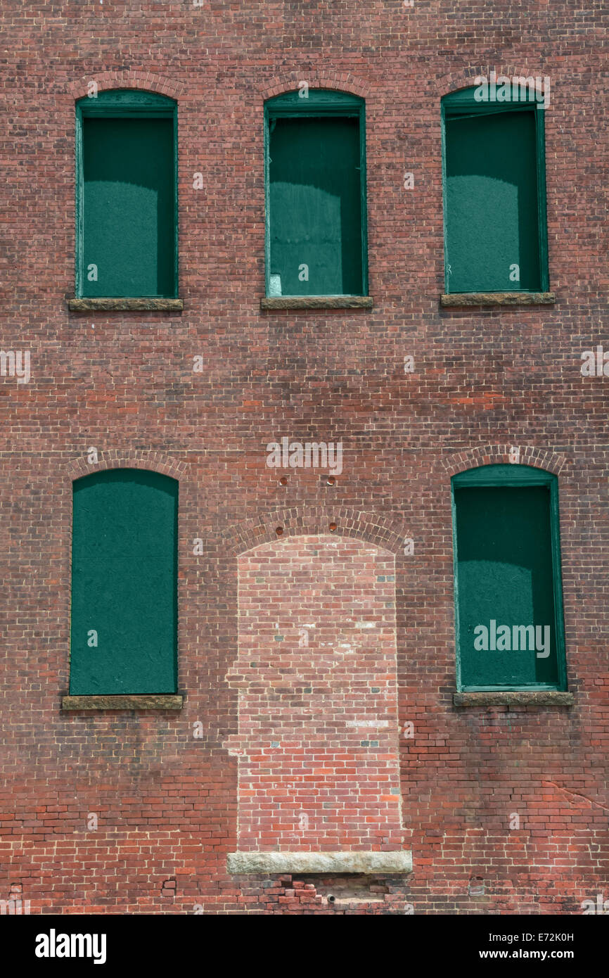 An abandoned factory wall with boarded windows and bricked in doorway ...