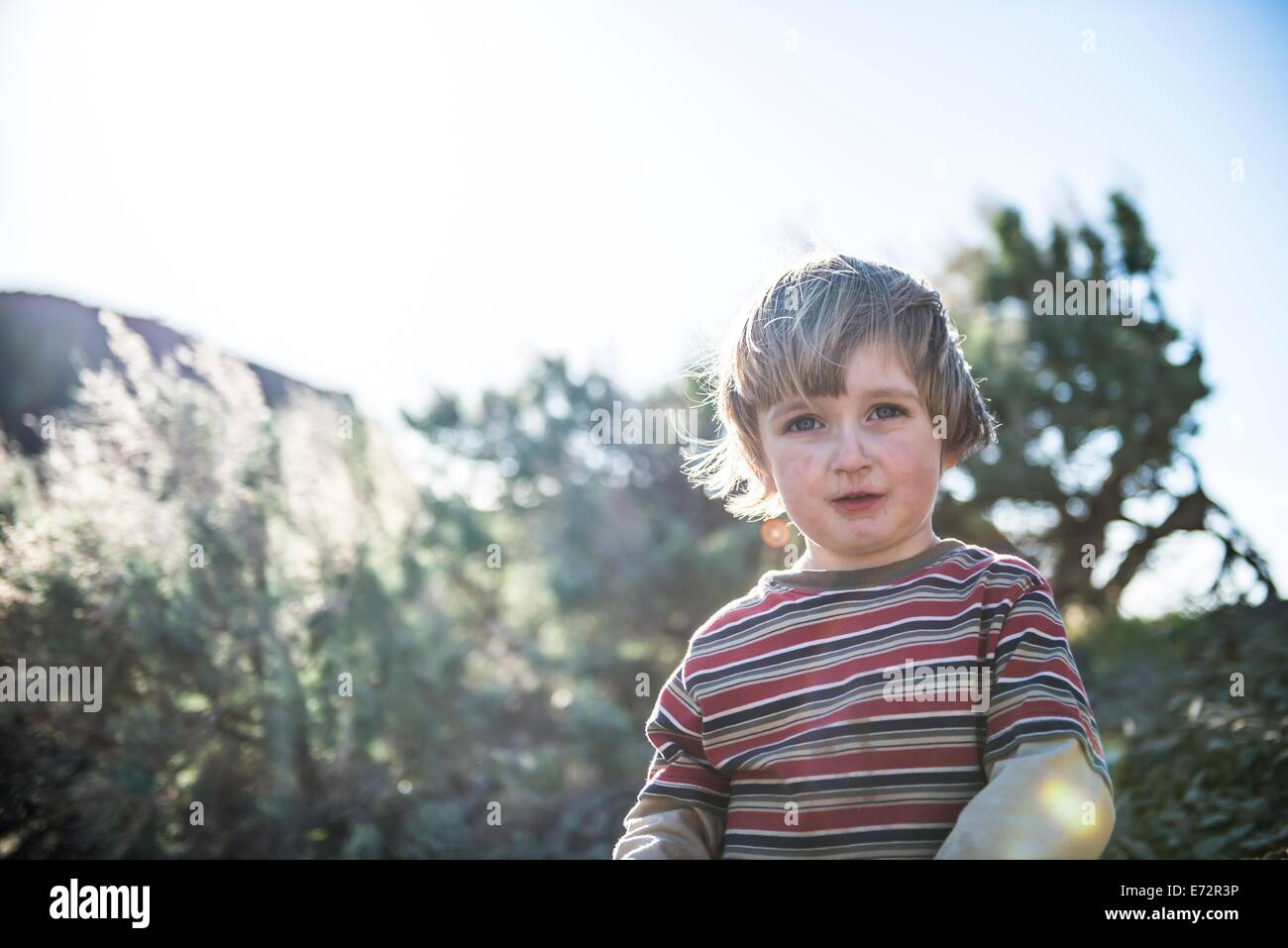 A young boy looks toward the camera with the sun shining in the ...