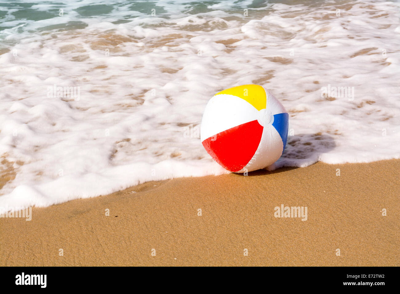 A colorful, summertime beach ball washes up to a sandy beach while ...